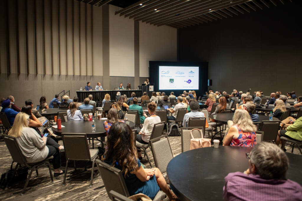 an audience made up primarily of city officials listens to a panel ...